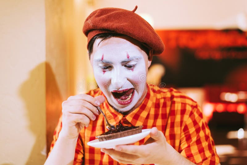 The Clown is Eating a Cake in a Cafe and His Face is Croaking. Stock ...