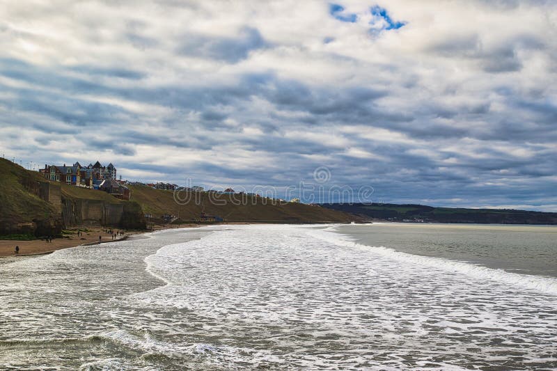 Coastal Scene with Beach, Town on Cliffs, and Cloudy Sky in Whitby, UK ...