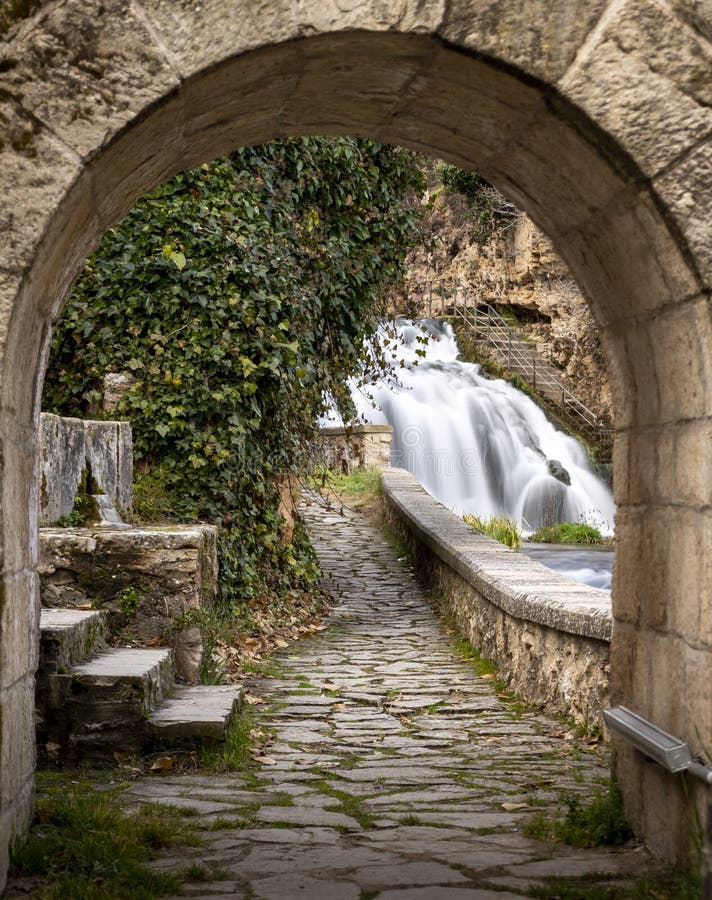 A Cobbled Path through an Arch with a Waterfall in the Background Stock ...