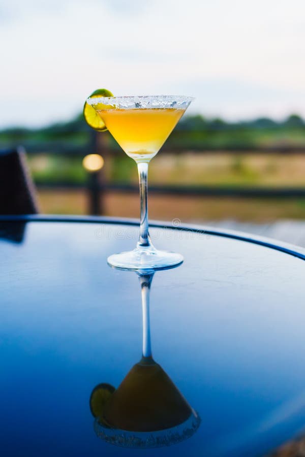 Cocktail Glass with a Lime Slice Sits on a Reflective Table at Sunset ...
