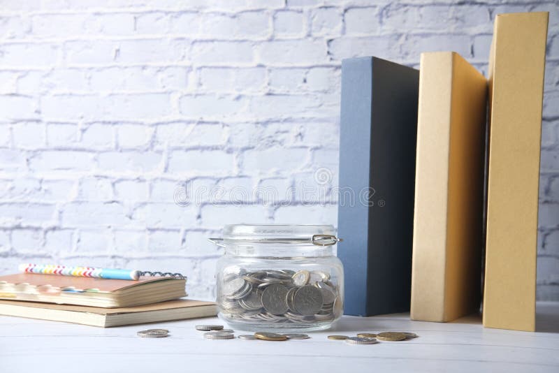 Coins in a Saving Jar and Stack of Book on Table Stock Image - Image of ...