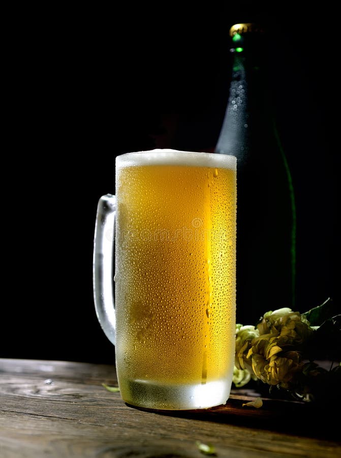 Cold Frothy Beer in Glass, Bottle and Hops on a Wooden Background Stock ...