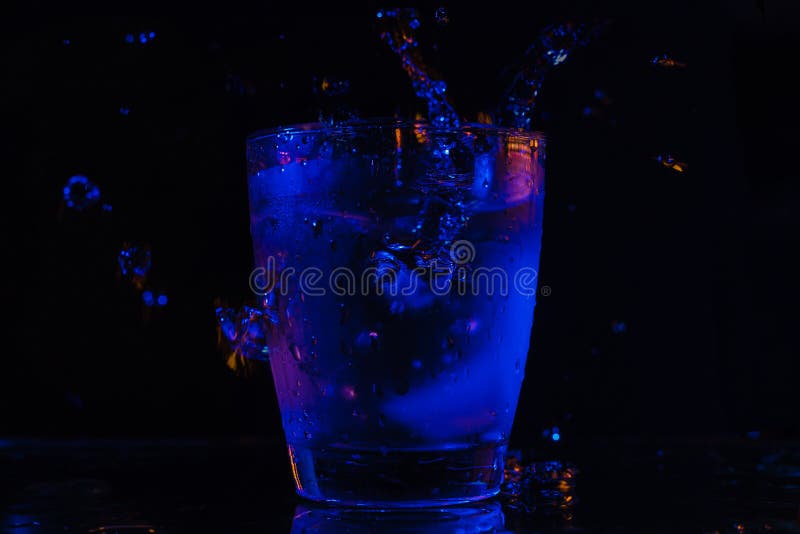 Cold Liquid Splash in a Glass on the Table Under the Colourful Lights ...