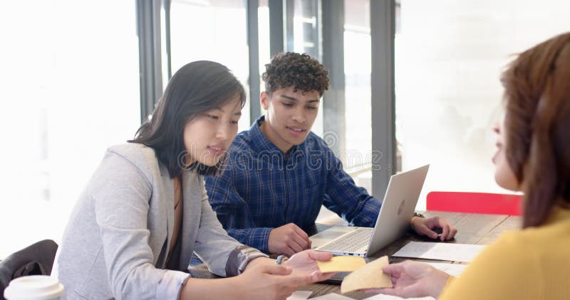 Collaborating on Project Details, Multiracial Colleagues Using Laptop and Documents in Office ...