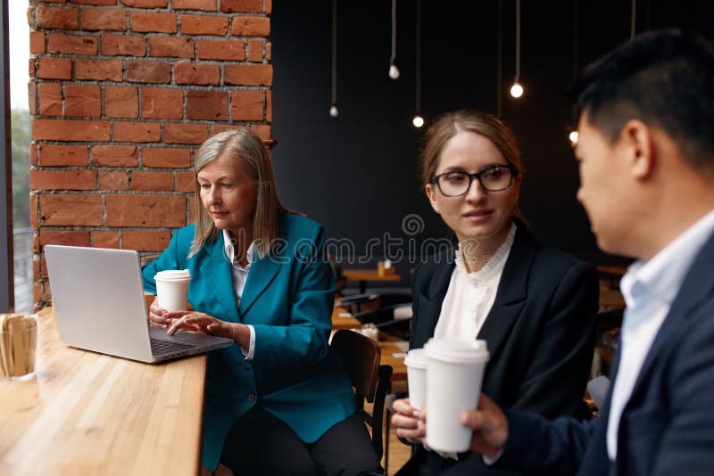 Colleagues Working Together at Cafe, Using Computer, Drinking Coffee ...