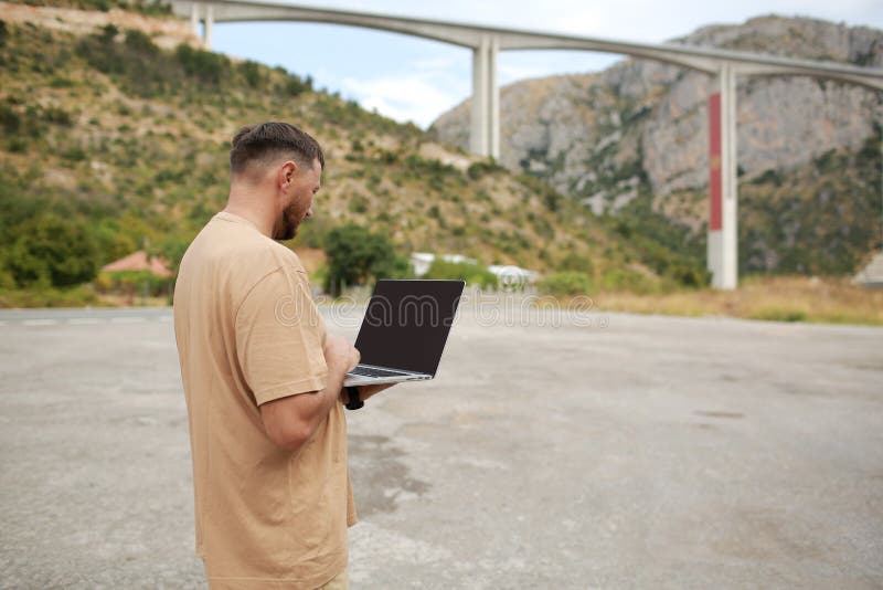 Collected Man in Casual Clothes Working on Laptop Outdoors on Bridge ...