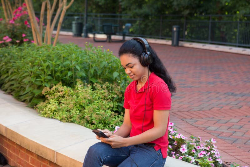 College Student with Headphones and Looking at a Cell Phone Stock Photo ...