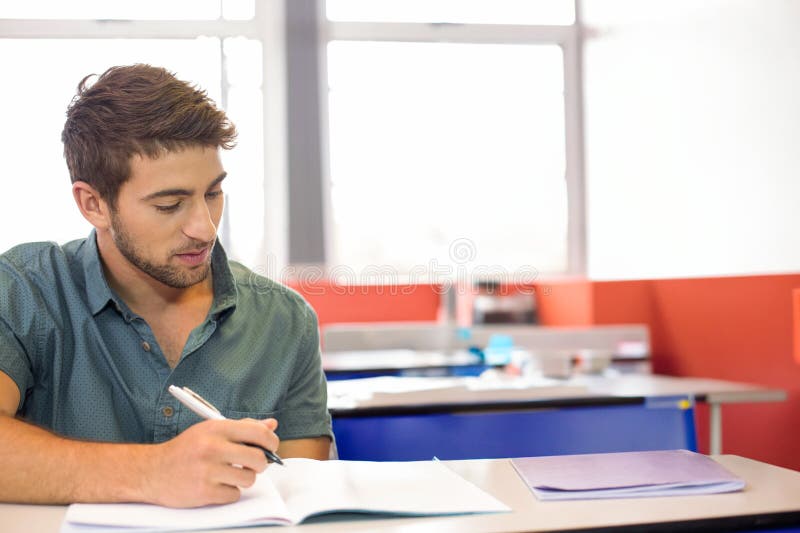 Male Student Sitting at Classroom Desk by Window Writing in Open ...