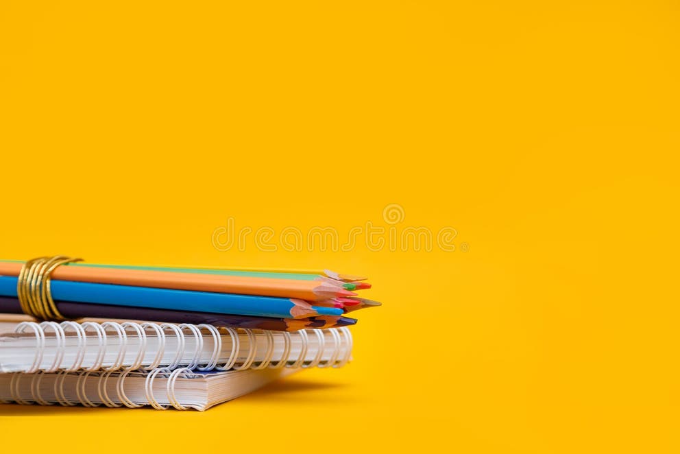 Colored Pencils on a Stack of Notebooks on a Yellow Background with ...