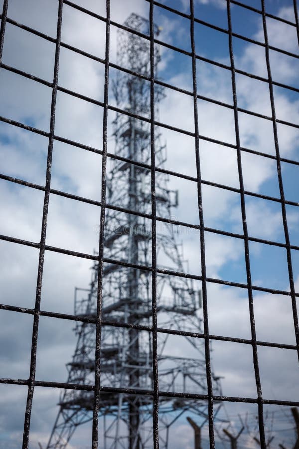 Communication Tower Behind Metal Grid Fence with Cloudy Sky, Depicting ...