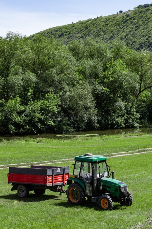 Compact Tractor on a Rural Lawn with Forest and River in the Background ...