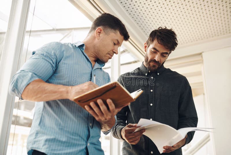 Comparing Notes. Two Handsome Young Businessmen Looking Over Their ...