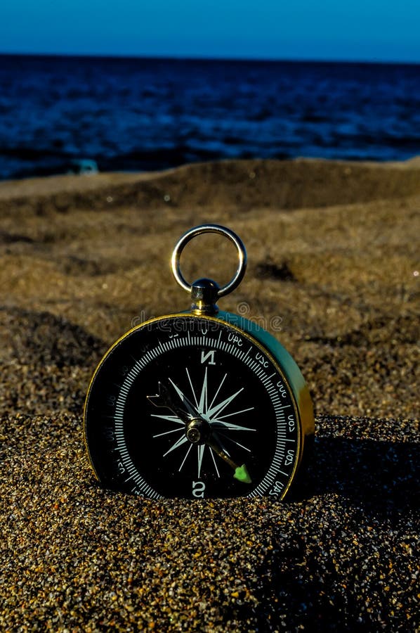 A Compass is Sitting on the Sand, with the Sand and Water in the ...