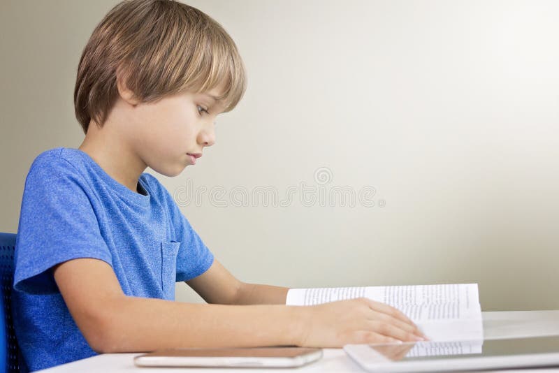 Concentrated Child Reading a Book. Mobile Phone and Tablet Computer are ...