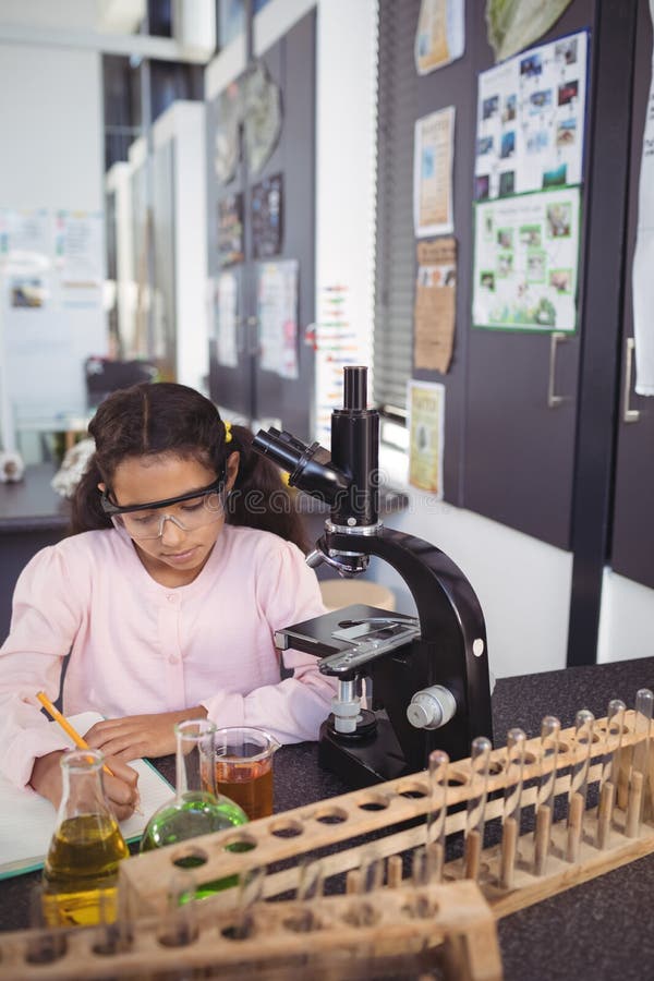 Concentrated Elementary Student Writing in Book by Microscope at ...