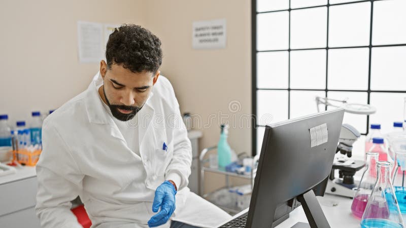 Concentrated Hispanic Man in Lab Coat Using Laptop in a Modern ...