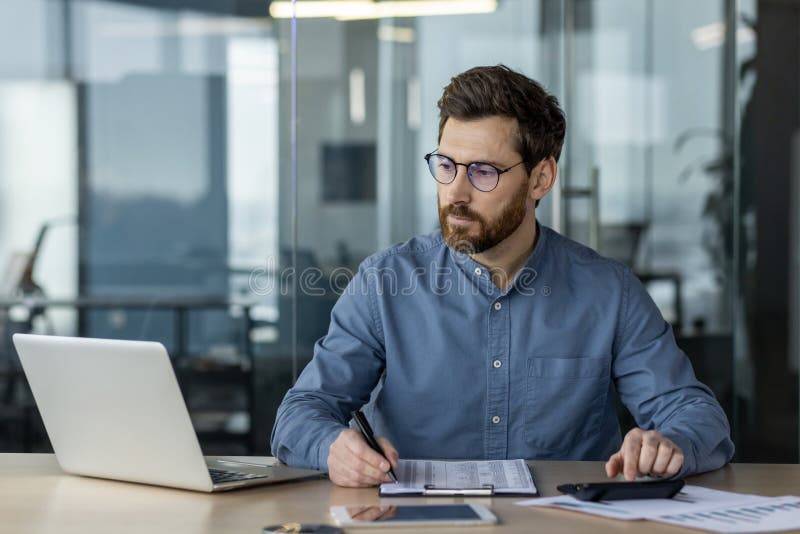 Concentrated and Serious Young Man Sitting in the Office at a Desk with ...