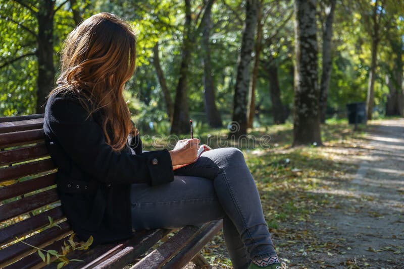 Concentrated Woman Writing on Notebook Sitting on a Bench in a Park ...