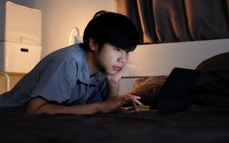 Concentrated Young Asian Man Working with Computer Laptop on His Bed ...