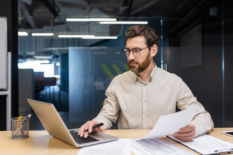 A Concentrated Young Man is Sitting in the Office at a Desk, Holding ...