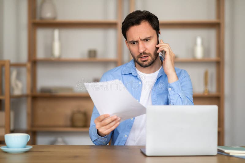 Concerned Man Reviewing Document while on Phone Call in Office Stock ...