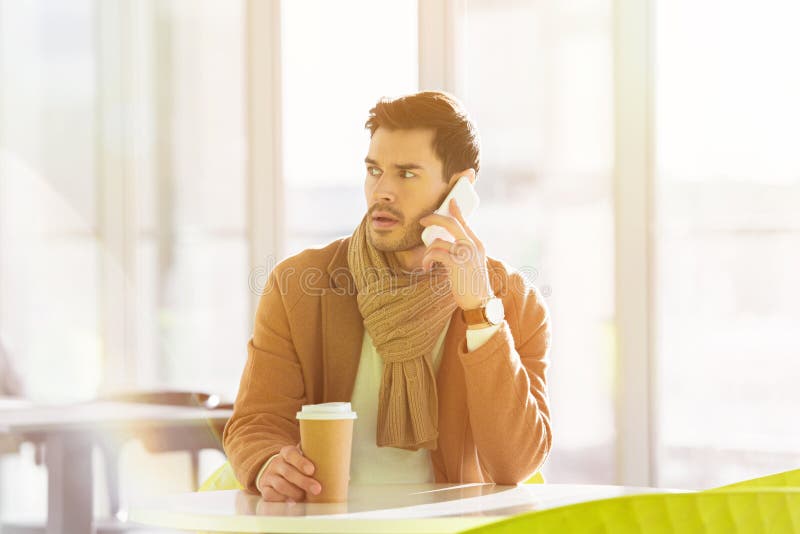 Concerned Man Sitting at Table, Holding Paper Cup and Talking on ...