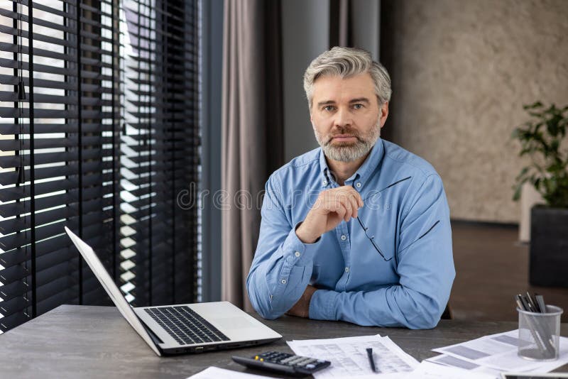 Confident Businessman at Desk Holding Glasses, Working on Laptop, and ...