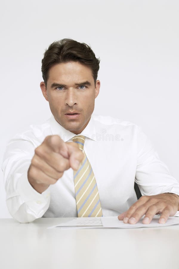 Confident Businessman Pointing while Sitting at Desk Stock Photo ...