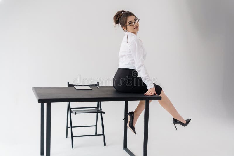 Confident Businesswoman Sitting on a Table Edge with a Notepad, Looking ...