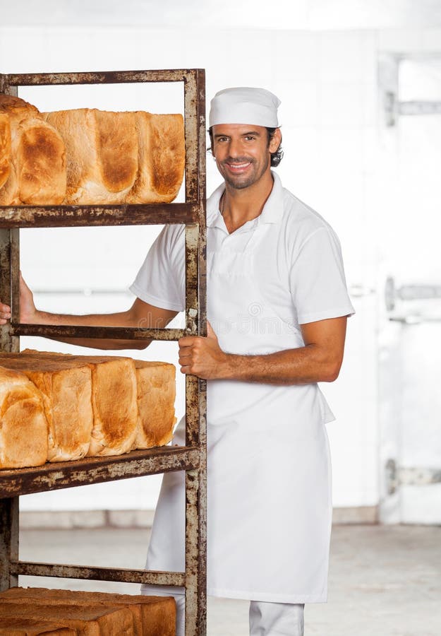 Confident Male Baker Standing by Bread Rack Stock Photo - Image of food ...