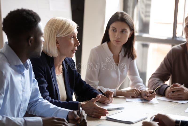 Confident Older Female Boss Team Leader Talking To Focused Workers