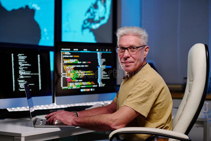 Confident Senior Male Programmer Looking At Camera By Workplace Stock