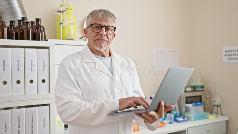 Confident Senior Male Scientist in Lab Coat Using Laptop in a Modern ...