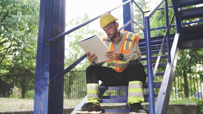 Tired Civil Engineer in Helmet and Safety Vest Sitting on Stairs with ...