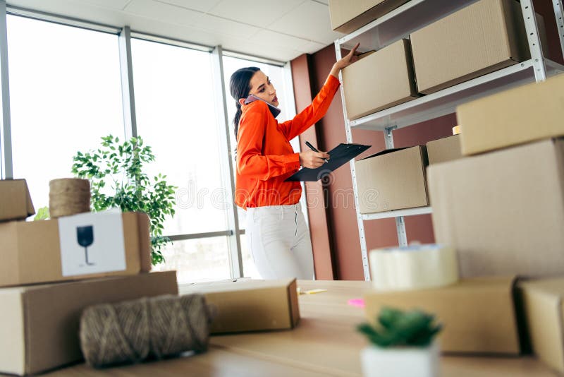 Professional Young Businesswoman Managing Orders in a Busy Workspace while Checking Documents ...