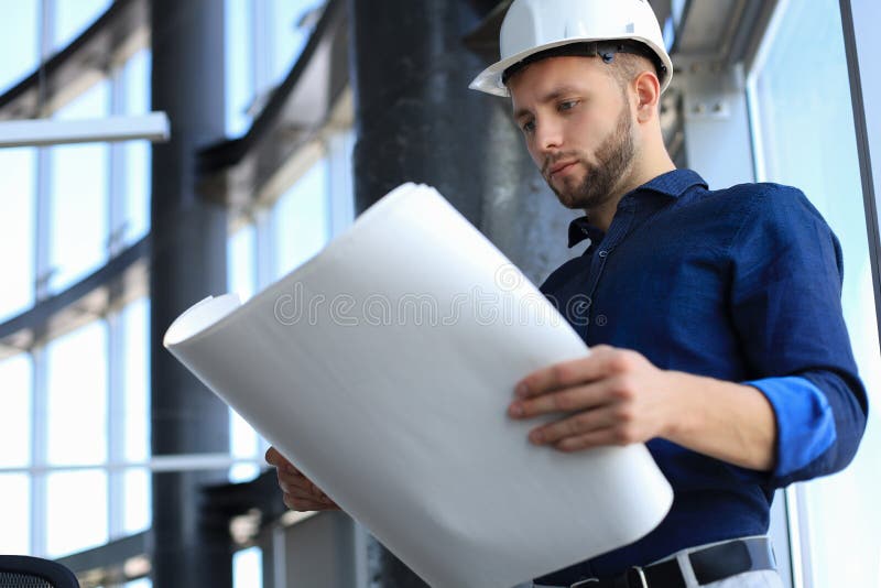 Confident Young Architect in Navy Shirt and Hardhat Holding a Blueprint ... Confident Young Architect in Navy Shirt and Hardhat Holding a Blueprint ...