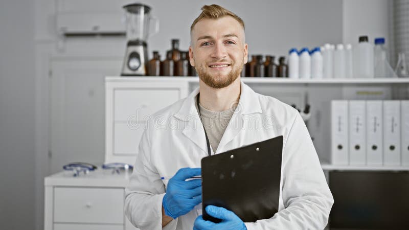 Confident Young Man with Beard in Lab Coat Holding Clipboard in a ...