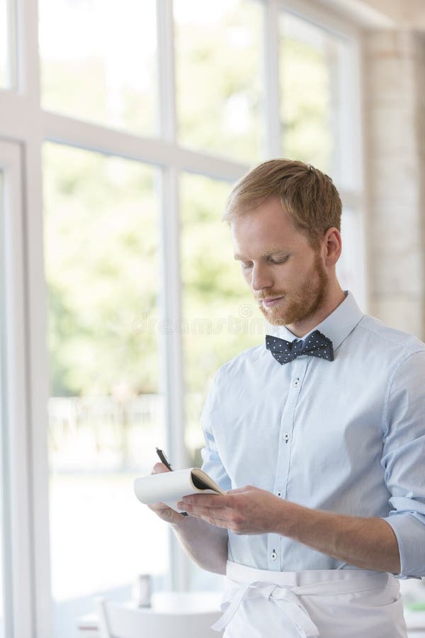 Confident Young Waiter Writing on Notepad while Standing at Restaurant ...