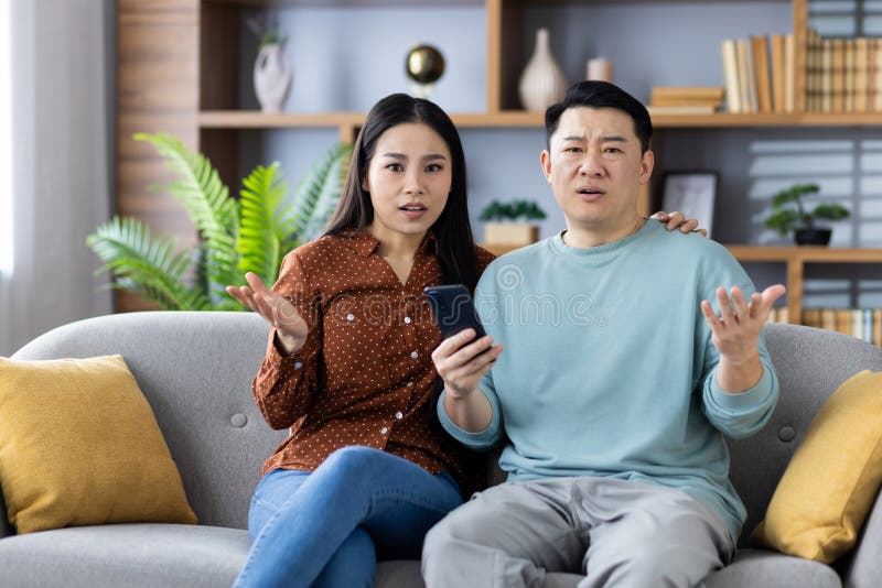 Confused Asian Couple Using Smartphone while Sitting on Sofa at Home ...