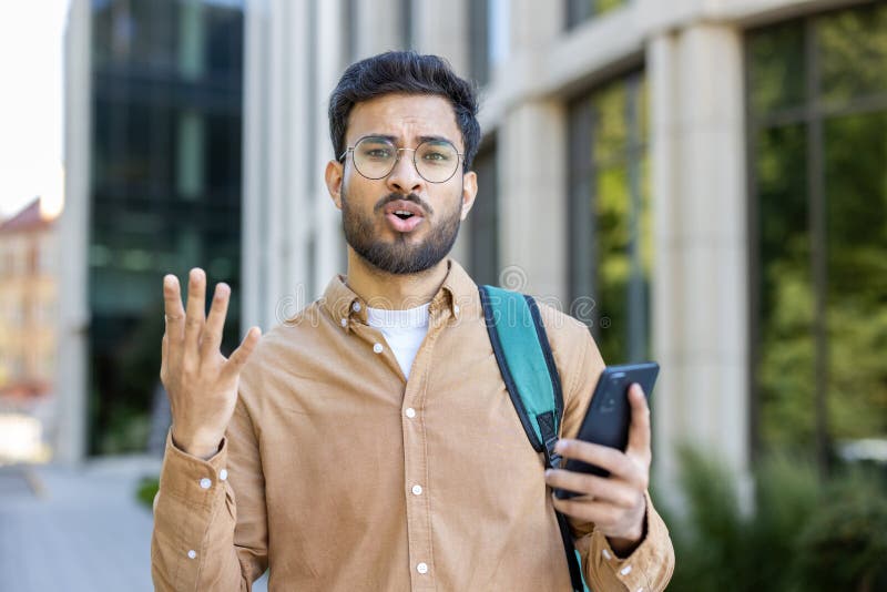 Confused Hispanic Student Holding Phone with Backpack Outside Modern ...