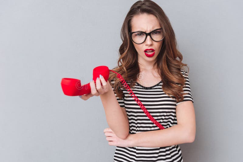 Confused Young Lady Standing Over Grey Wall Holding Phone. Stock Image ...