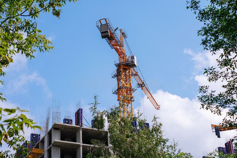 A Construction Crane Works Against a Blue Sky and an Unfinished ...