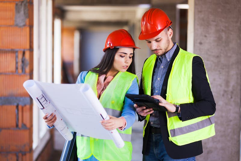 Team of Engineers in Vests and Hard Hats with Schematics on a ...