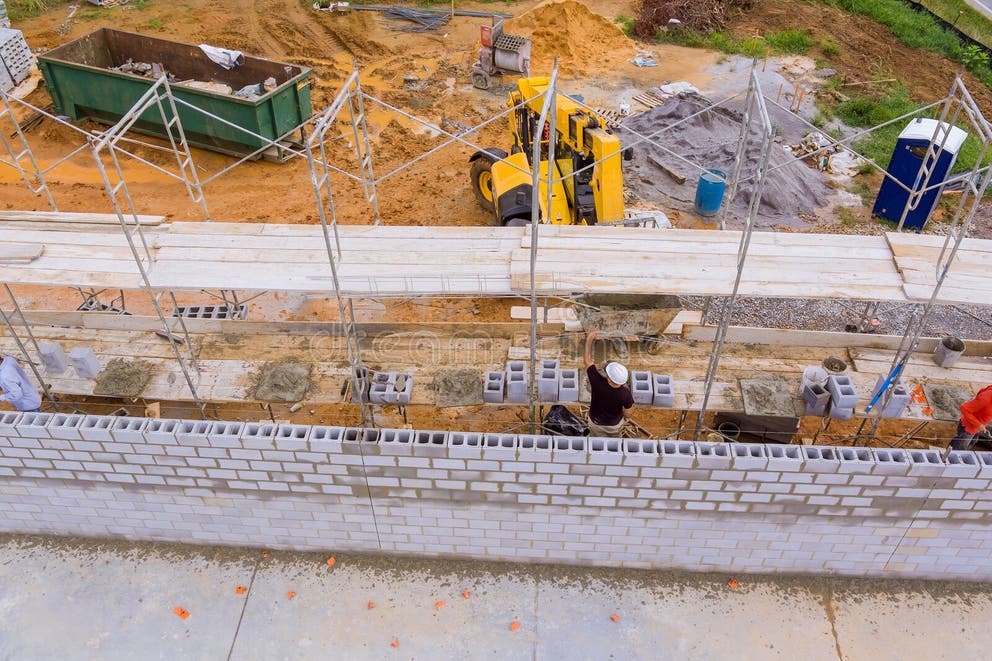 On Construction Site, Mason Stands on Scaffolding Constructs a Concrete Wall Using Cement Blocks ...