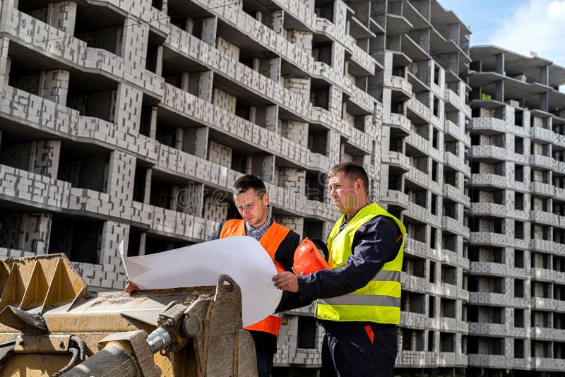 On a Construction Site, One Worker in Uniform Shows Another Worker in ...