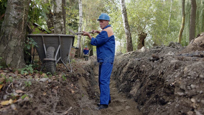 A Construction Worker is Digging a Trench in the Forest with a ...