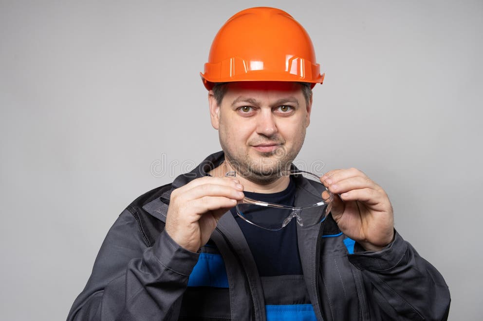 A Construction Worker in a Helmet and Overalls Put on Goggles ...