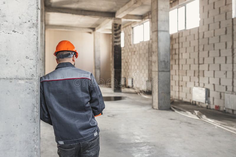 A Construction Worker in a Helmet Stands with His Back To the Camera ...