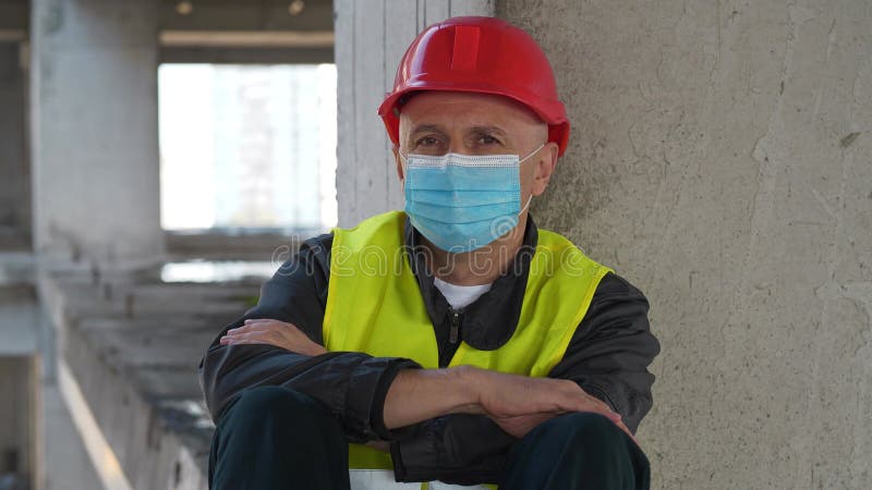 Construction Worker in Protective Face Mask Sits on the Floor and Look ...