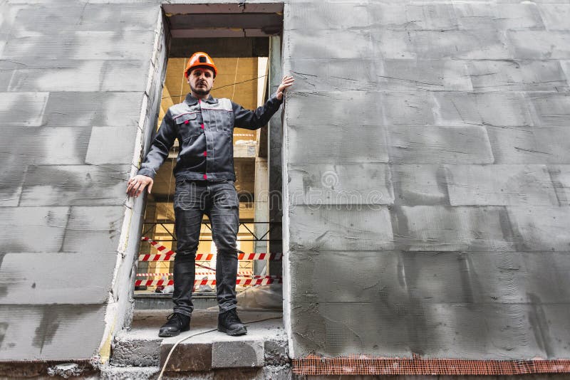 A Construction Worker in Overalls Stands in the Opening of a Building ...